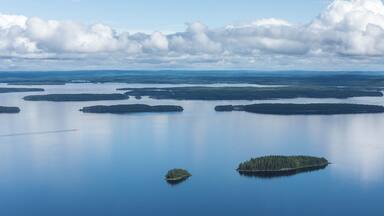 Um lago tranquilo com várias ilhas, cercado por uma paisagem arborizada e um céu nublado.