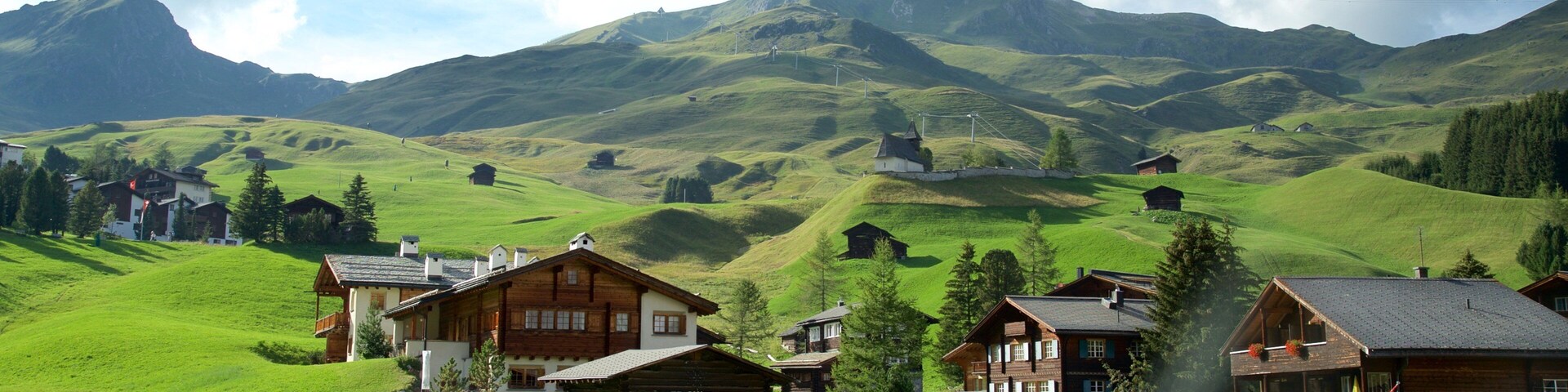 Uma aldeia com casas de madeira, uma escola infantil e uma montanha ao fundo.