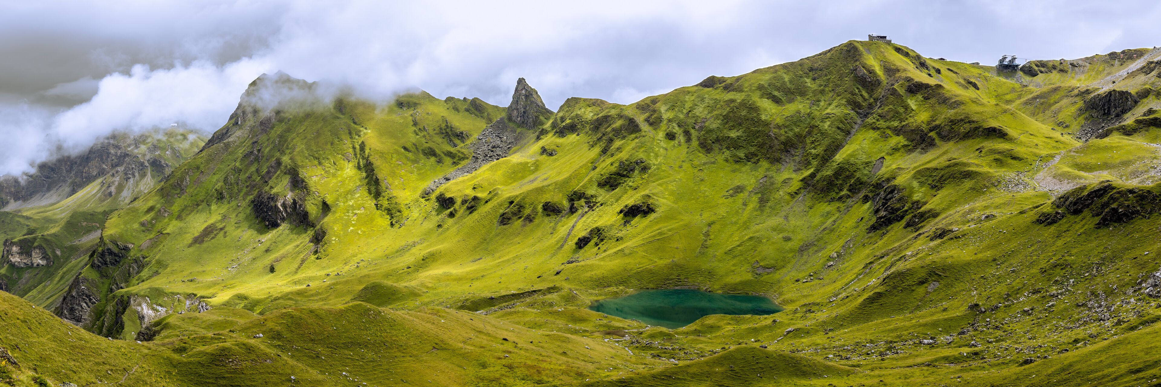 Paisagem montanhosa com um pequeno lago e um mirante numa colina.