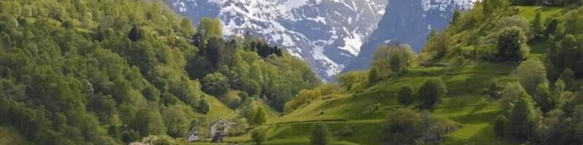 Um vale verde com casas e um lago, rodeado por montanhas cobertas de neve.