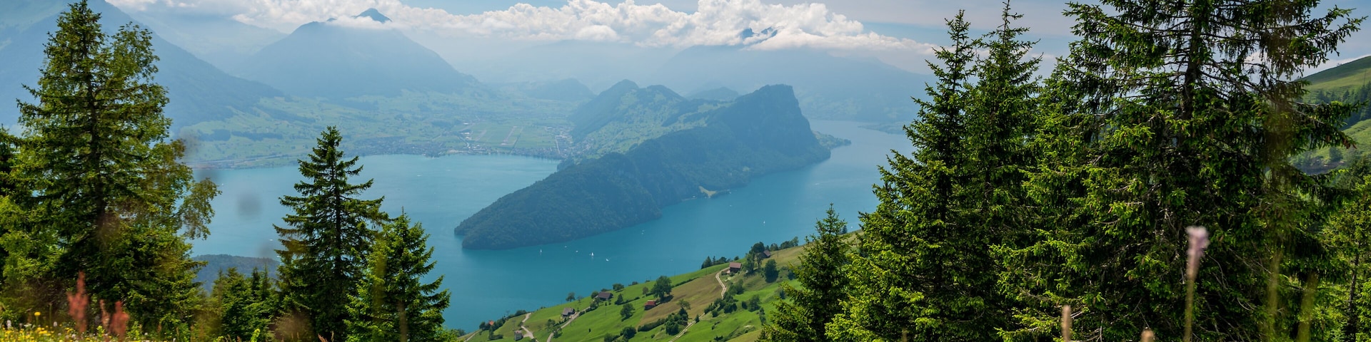 Paisagem montanhosa com um lago, florestas densas e um céu azul límpido.