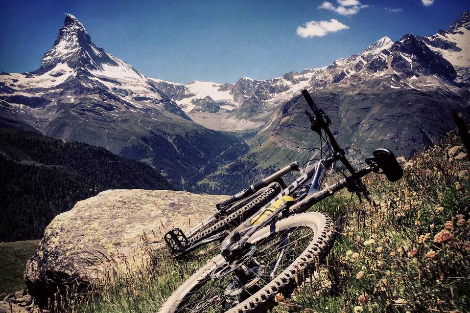 Uma bicicleta de montanha encostada em uma rocha, com uma montanha nevada ao fundo.