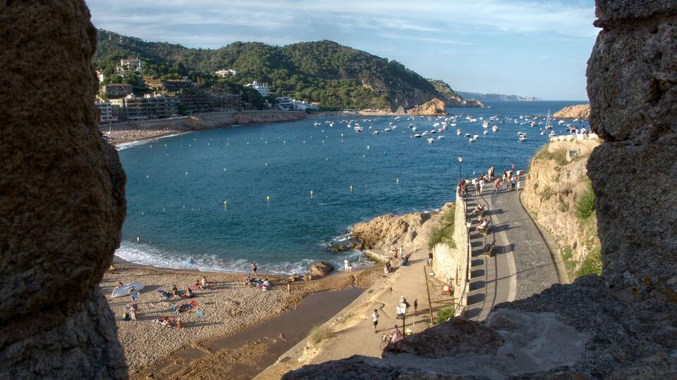 Uma cidade costeira com praia, falésias rochosas e barcos na água.