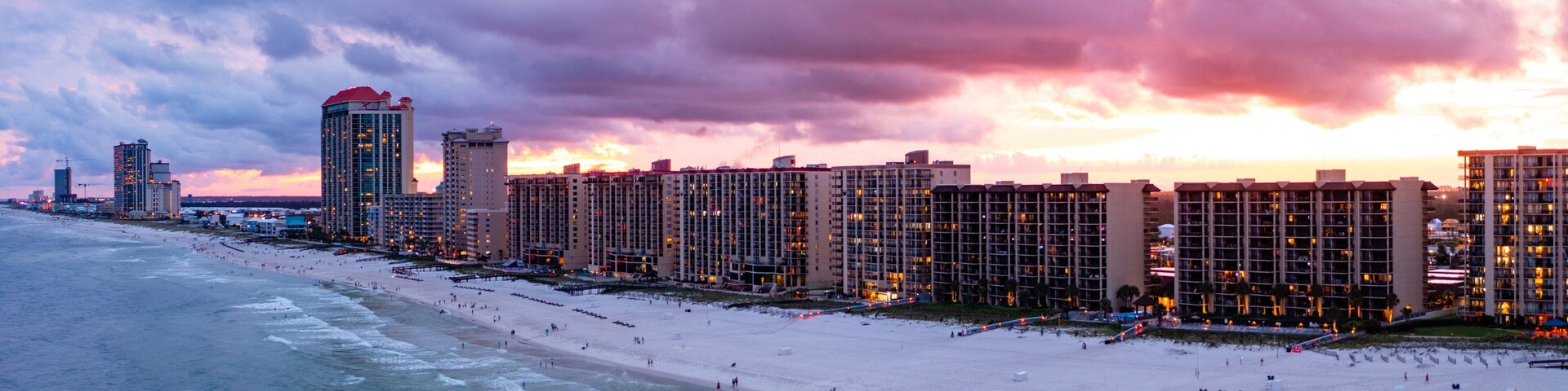 Paisagem costeira com praia, edifícios altos e céu ao pôr do sol.