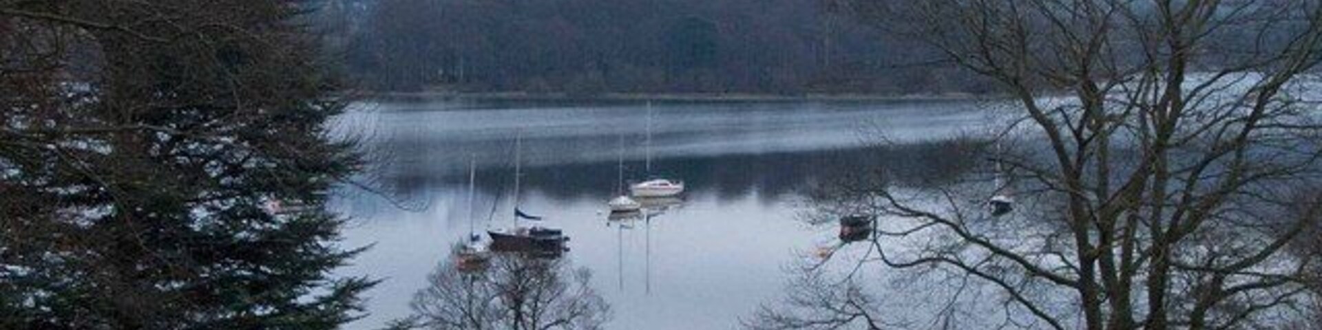 Um lago com barcos, um cais e uma montanha ao fundo.