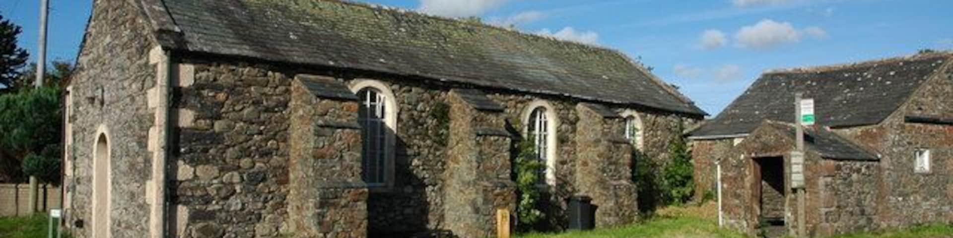 Igreja de pedra com chaminé, janelas em arco e uma estrada na frente.