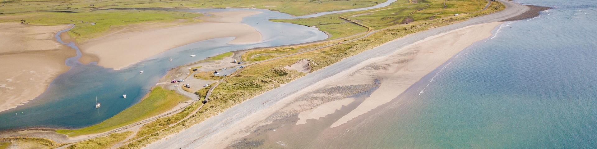 Paisagem costeira com uma praia de areia, a foz de um rio e uma cidade ao longe.