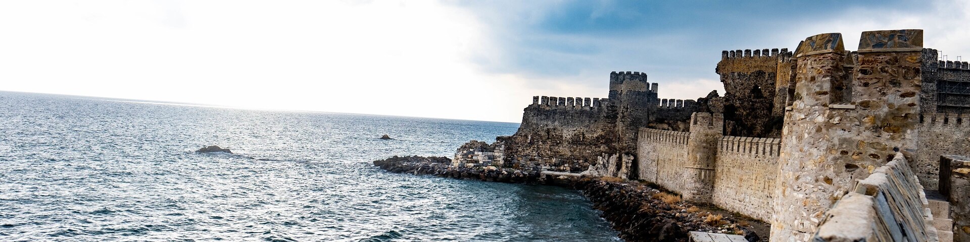 Um castelo à beira-mar com uma muralha de pedra e torres sobre o oceano.