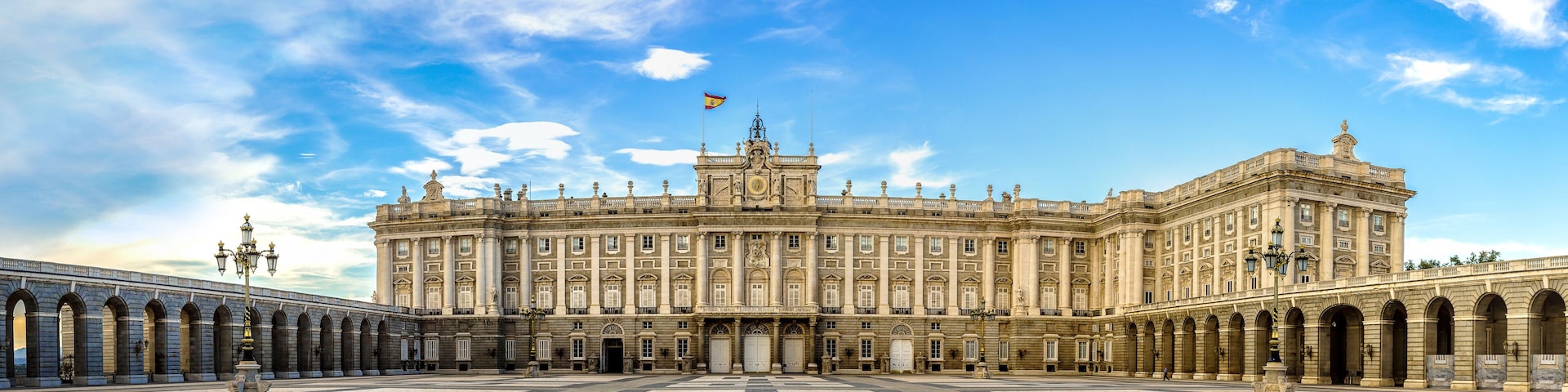 Um edifício histórico imponente com fachada simétrica, grandes portas centrais e um mastro.