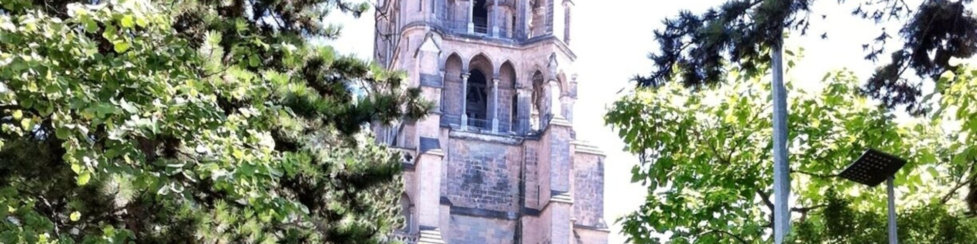 Um edifício histórico com uma torre, rodeado por vegetação exuberante e uma escadaria que o leva até ele.