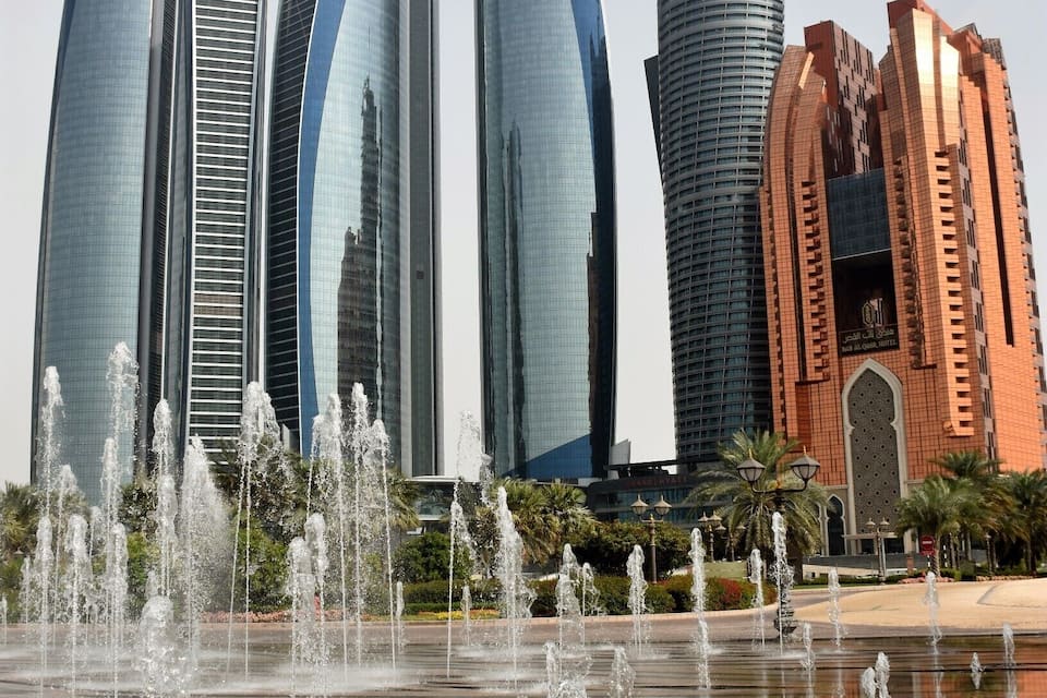 Paisagem urbana moderna com arranha-céus imponentes e uma fonte em primeiro plano.