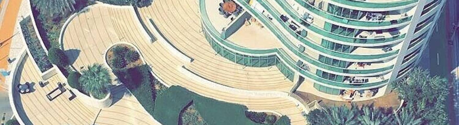 Um edifício alto com fachada curva, um pátio central com piscina circular e vegetação ao redor.