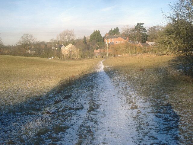Paisagem rural com um caminho estreito, casas e campos abertos.