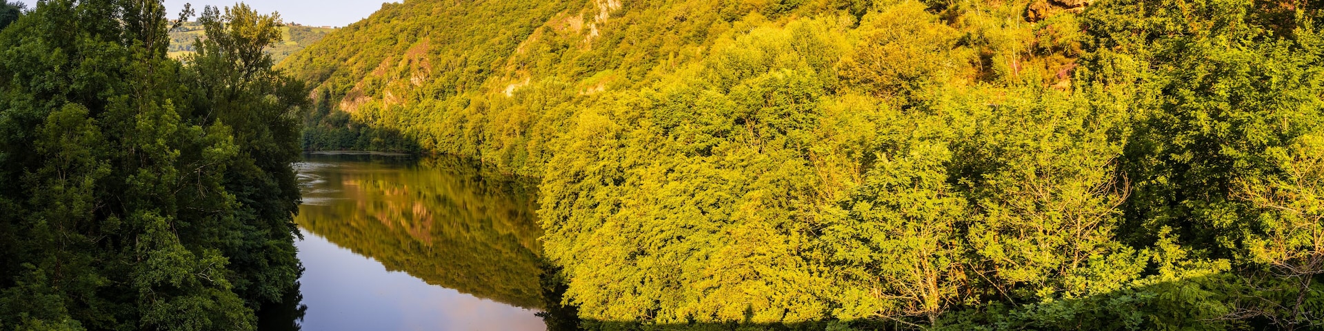 Um rio tranquilo refletindo a vegetação exuberante e as colinas ao redor.