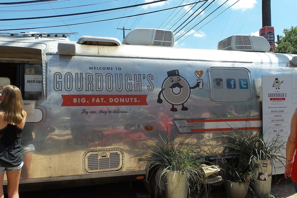 Um food truck com a marca 'Gourdhough's Big Fat Donuts' e uma ilustração de personagem.