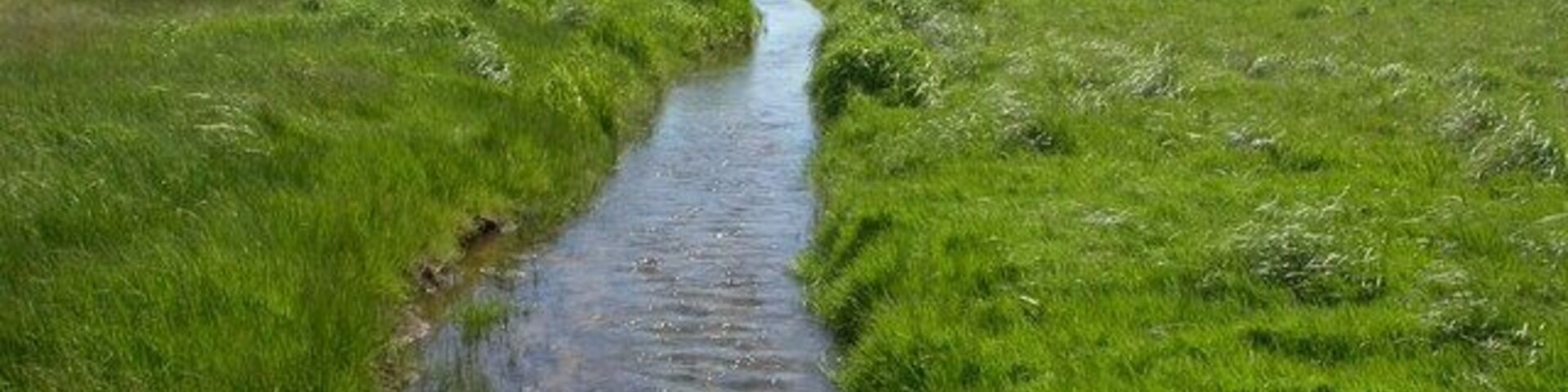 Um estreito canal de água em um campo gramado sob um céu claro.