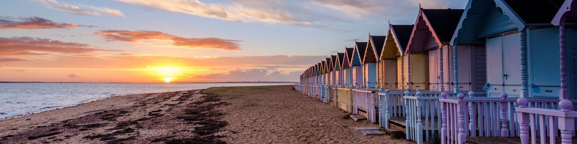 Uma praia com cabanas de madeira e um pôr do sol.