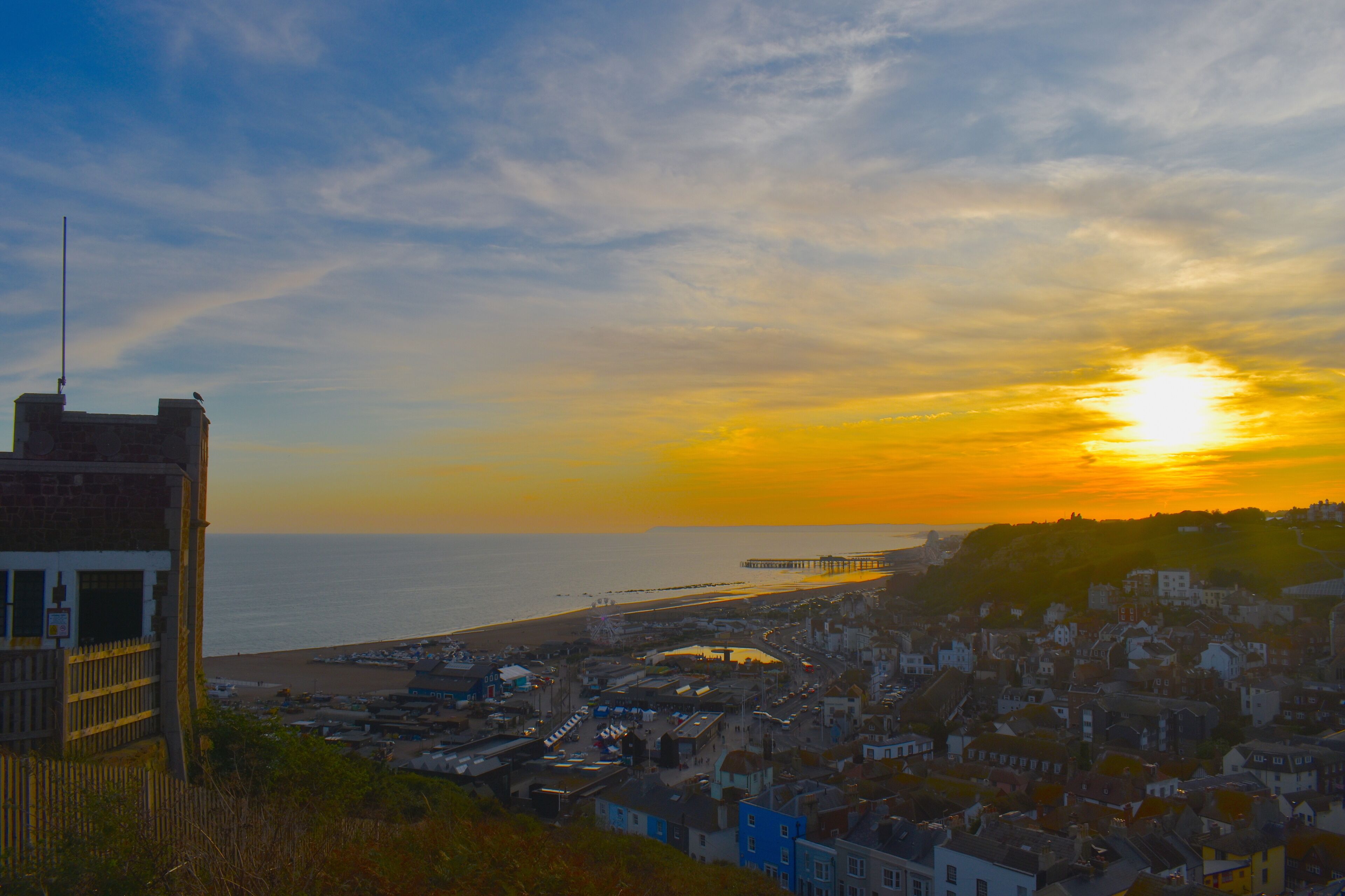 Uma cidade costeira ao pôr do sol, com céu claro, uma praia e um píer que se estende para o mar.