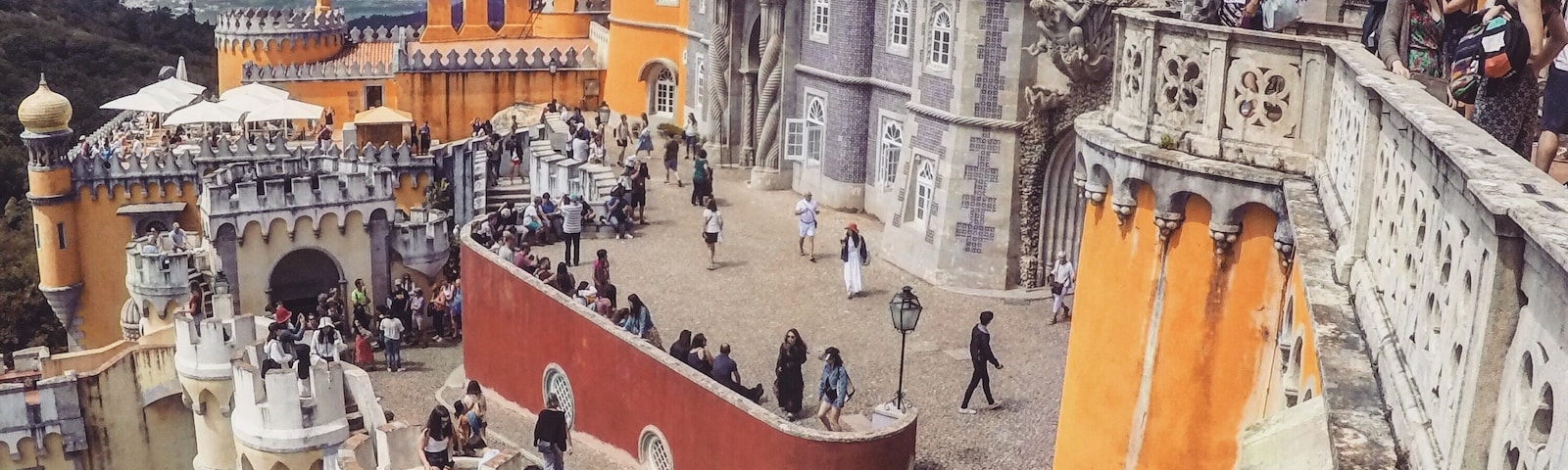 Um castelo histórico com múltiplas torres e cúpulas, cercado por uma grande multidão de visitantes.