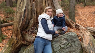 Uma mulher e uma criança sentadas sobre uma rocha grande numa floresta, com um tronco de árvore imponente ao fundo.