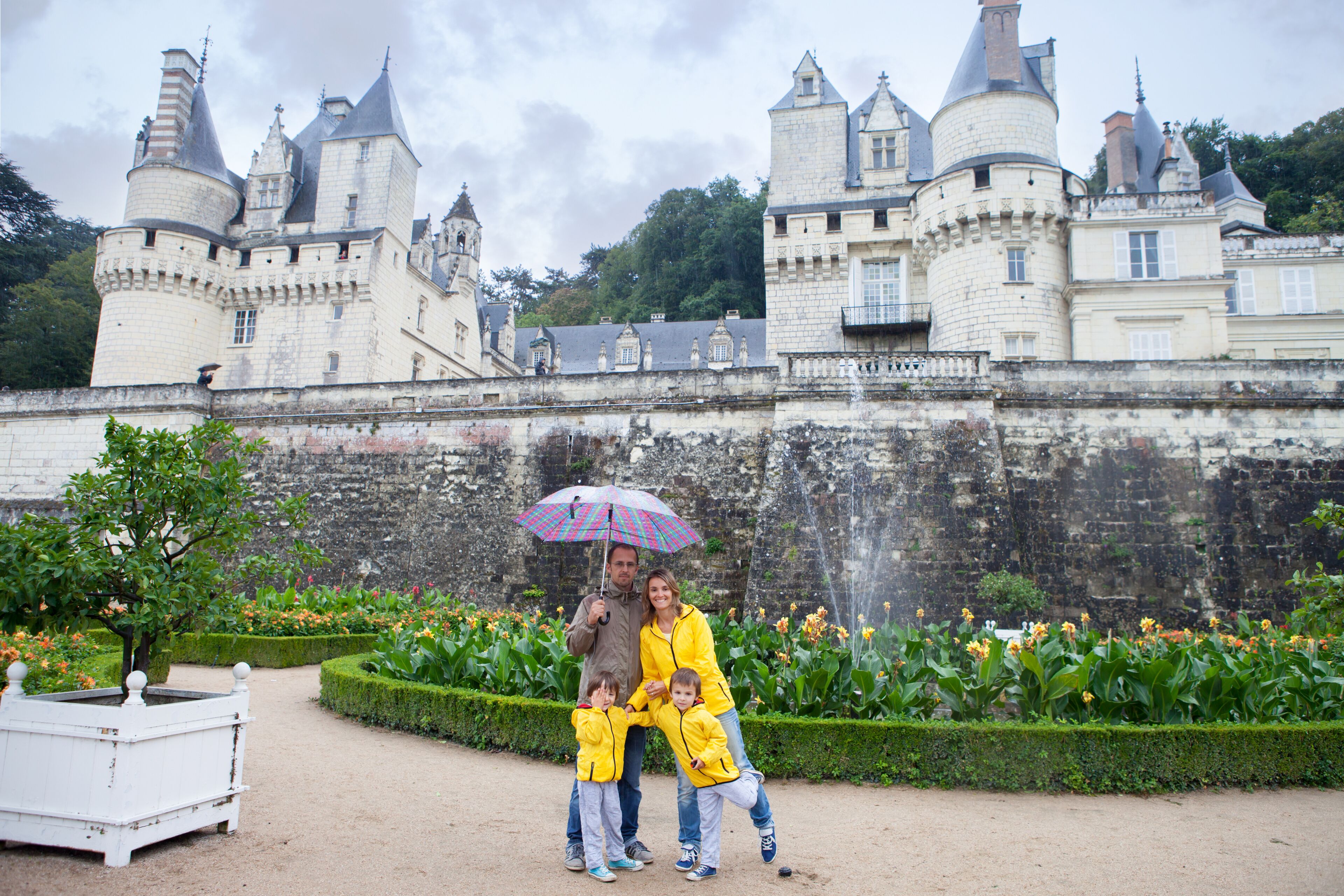 Um castelo histórico com várias torres e um jardim bem cuidado, com flores e sebes.