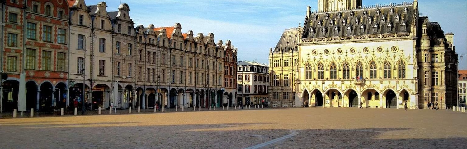 Uma praça histórica com calçamento de pedra, uma imponente torre do relógio e arquitetura clássica.