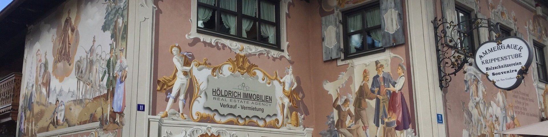 Um edifício com uma placa de imobiliária, um relógio e uma loja com diversos artigos.