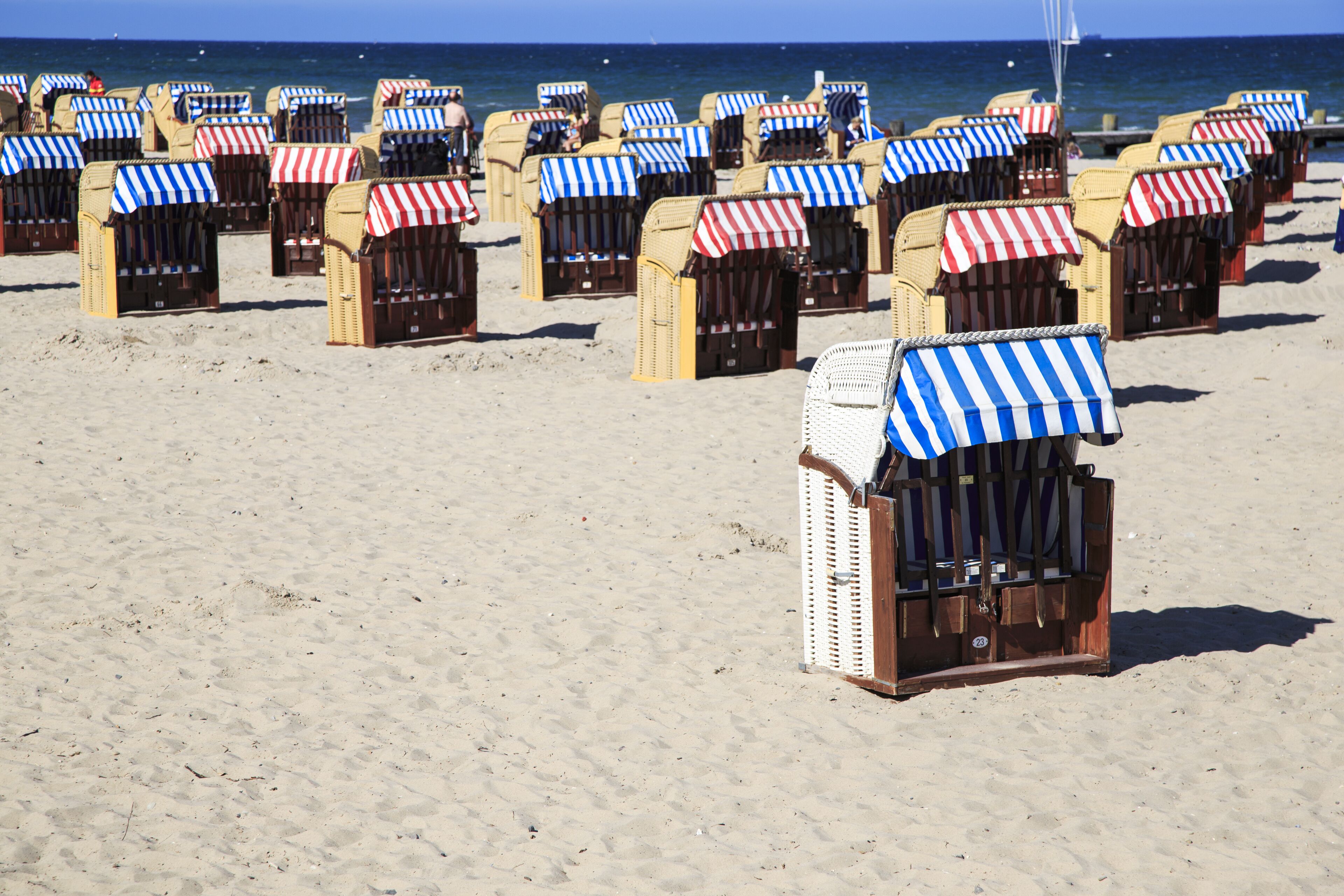 Fileiras de cadeiras de praia com guarda-sóis listrados numa praia de areia.