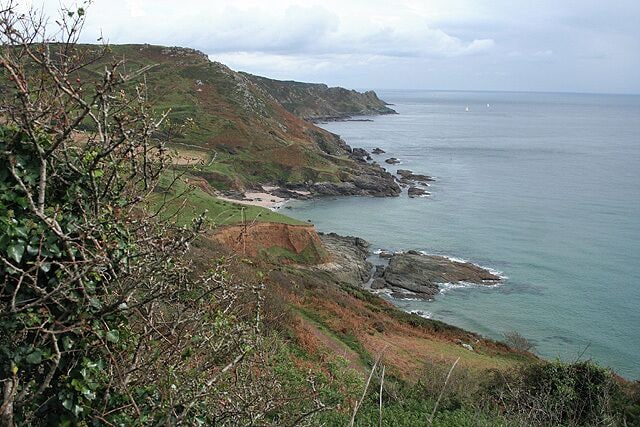Paisagem costeira com falésias rochosas, uma praia e vista do oceano.