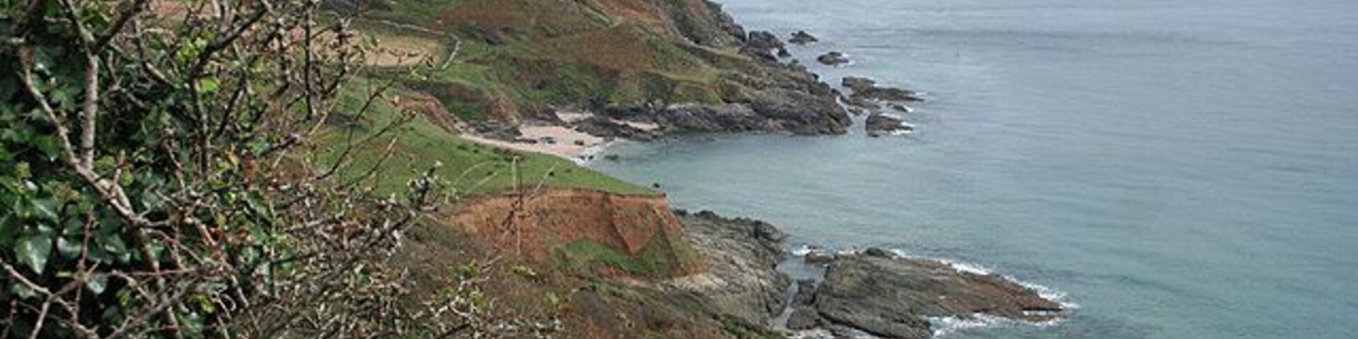 Paisagem costeira com falésias rochosas, uma praia e vista do oceano.