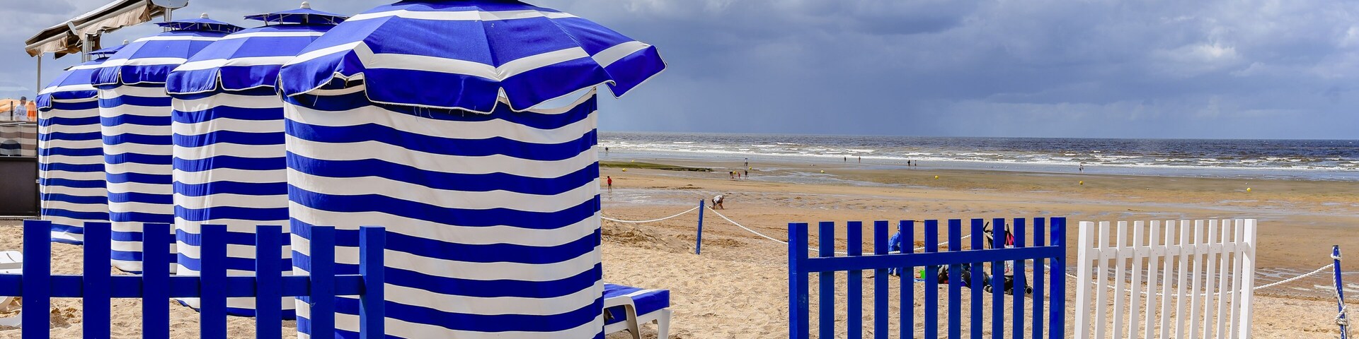 Uma praia com guarda-sóis listrados e uma cerca azul.