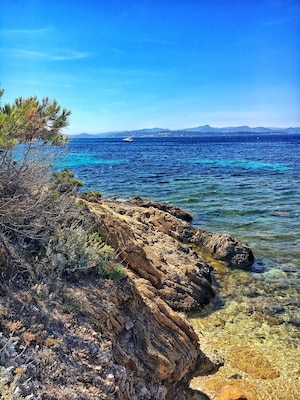 Costa rochosa com águas azul-claras e montanhas ao longe.