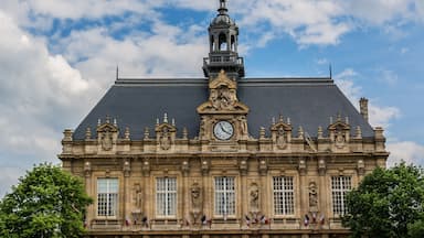 Um edifício histórico com uma torre do relógio, estátuas e bandeiras.