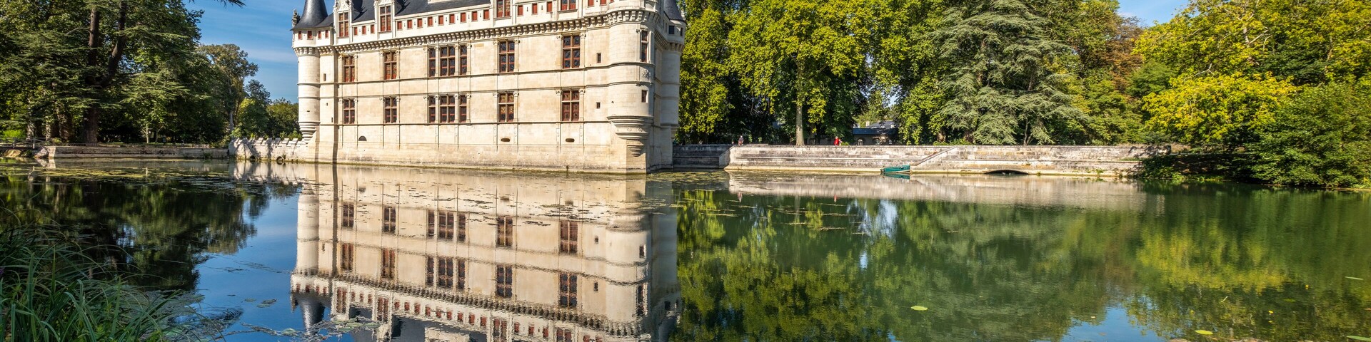 Um castelo histórico com fossado, rodeado por vegetação exuberante e árvores.