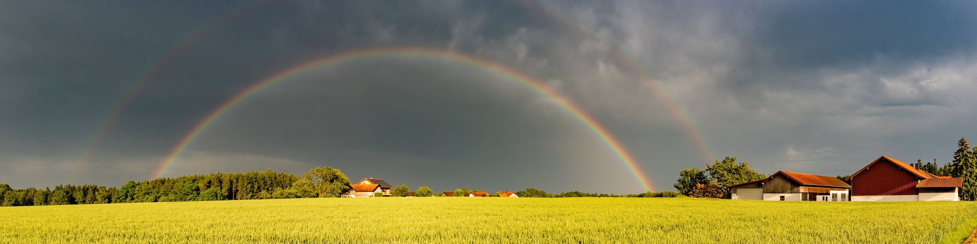 Um campo com um arco-íris, uma casa de fazenda e um celeiro.