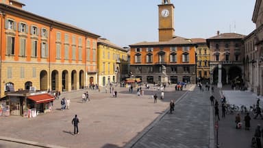 Uma praça histórica com uma torre do relógio imponente, edifícios coloridos e um espaço aberto no centro.