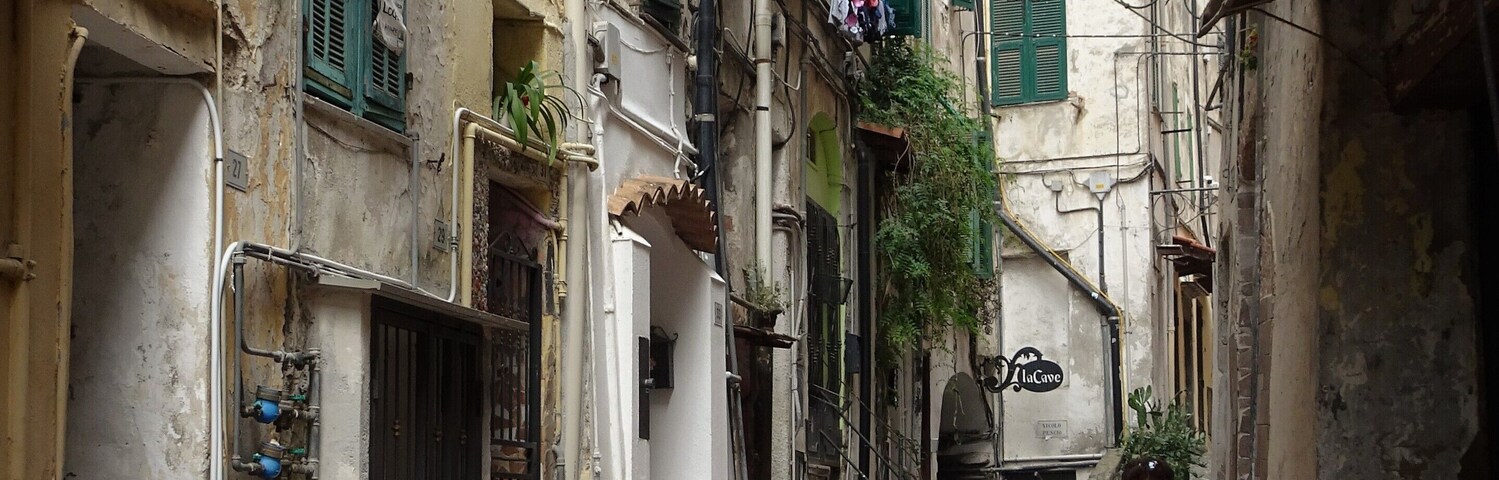 Um beco estreito com edifícios antigos, persianas verdes e uma placa com o nome "LaCave".