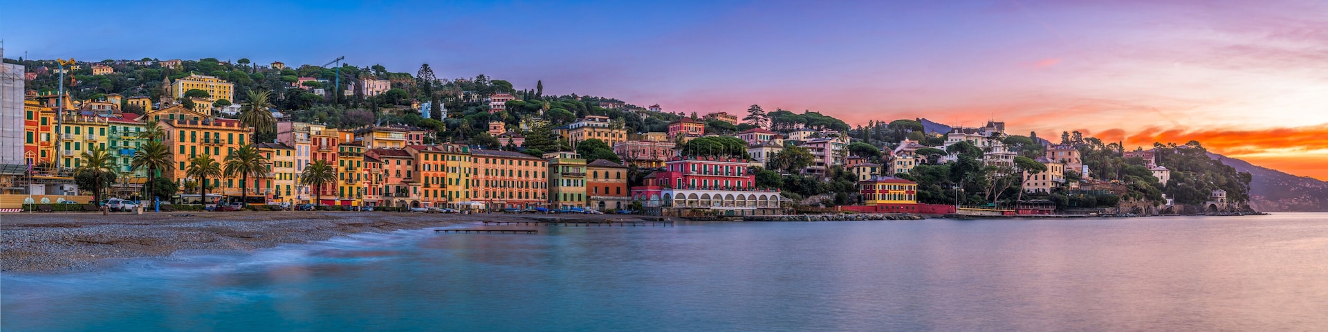 Uma vila costeira com edifícios coloridos e um mar calmo ao pôr do sol.