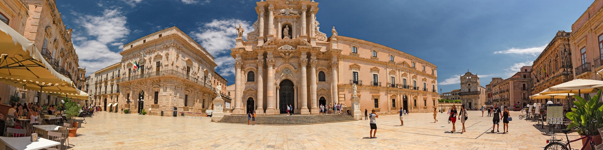 Uma praça histórica com uma igreja imponente, dotada de uma torre de sino e estátuas.