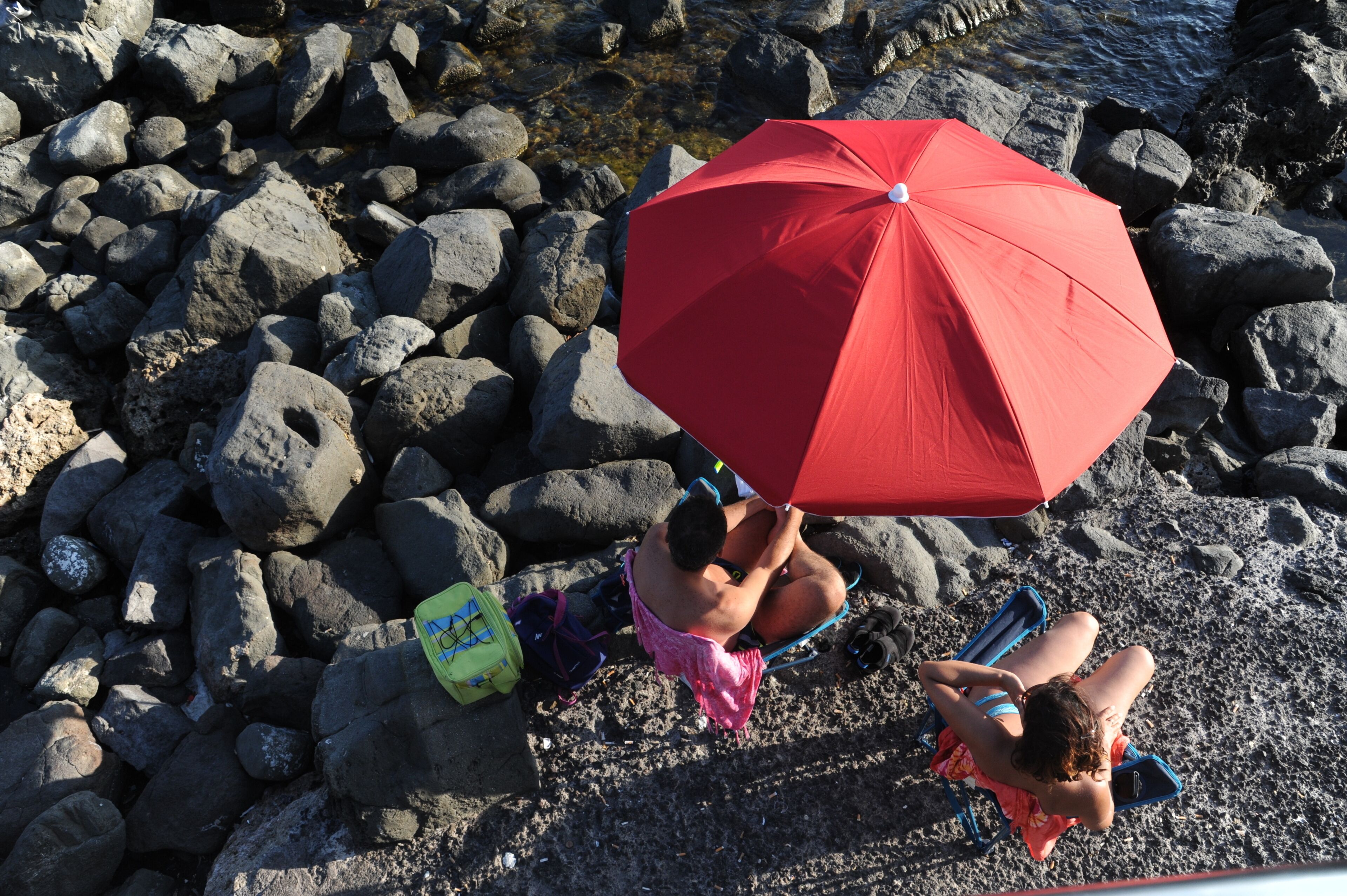 Uma praia rochosa com um guarda-sol vermelho que oferece sombra.