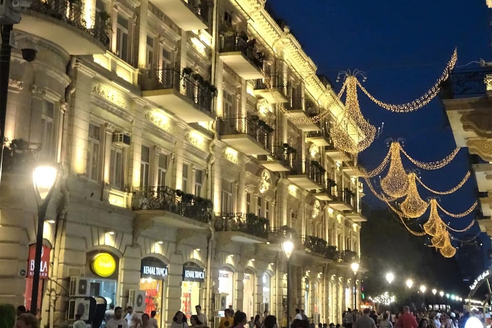 Uma rua movimentada à noite, com prédios iluminados e uma grande estrutura dourada decorativa.
