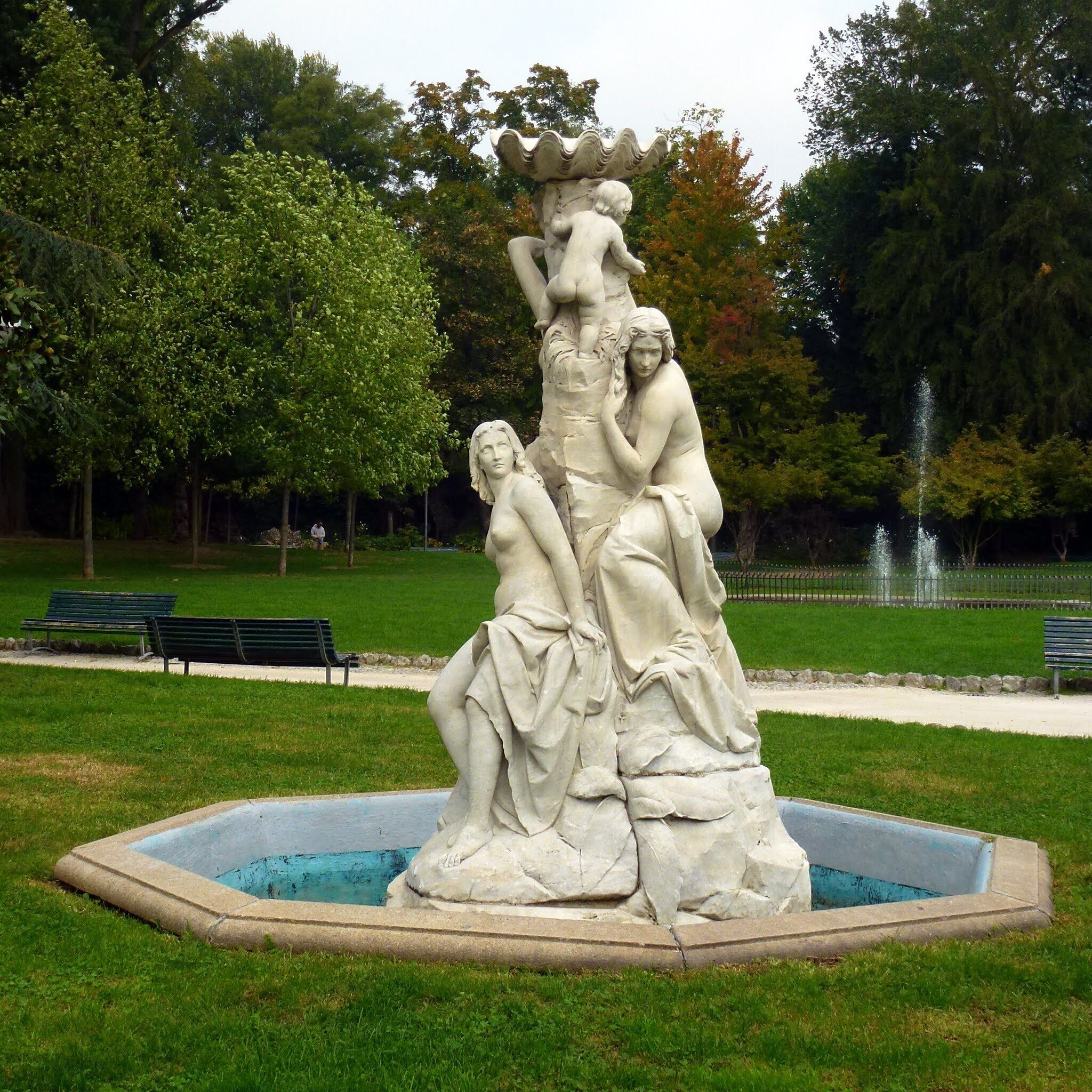 Escultura cl ássica em um parque com bancos e uma fonte.