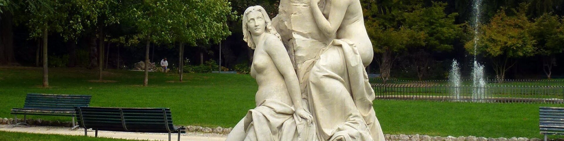 Escultura clássica em um parque com bancos e uma fonte.