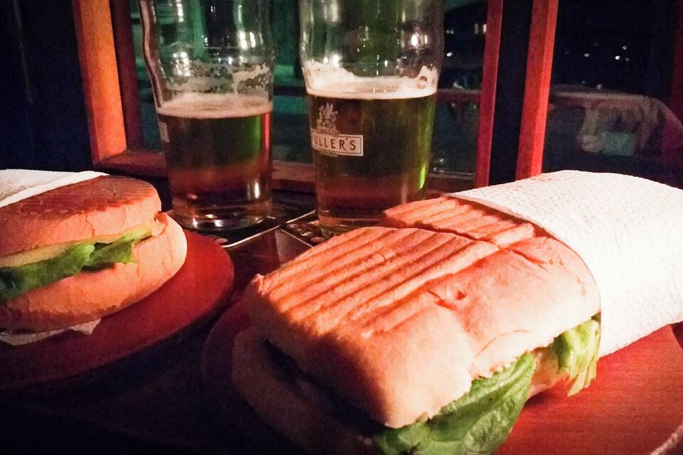 Dois sanduíches e dois copos de cerveja sobre uma mesa de madeira.