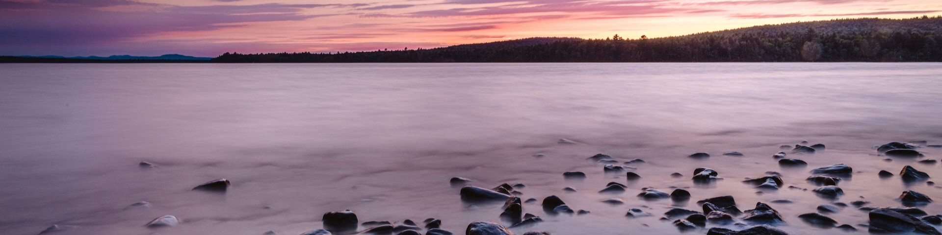 Um lago calmo com rochas espalhadas e um céu ao pôr do sol.