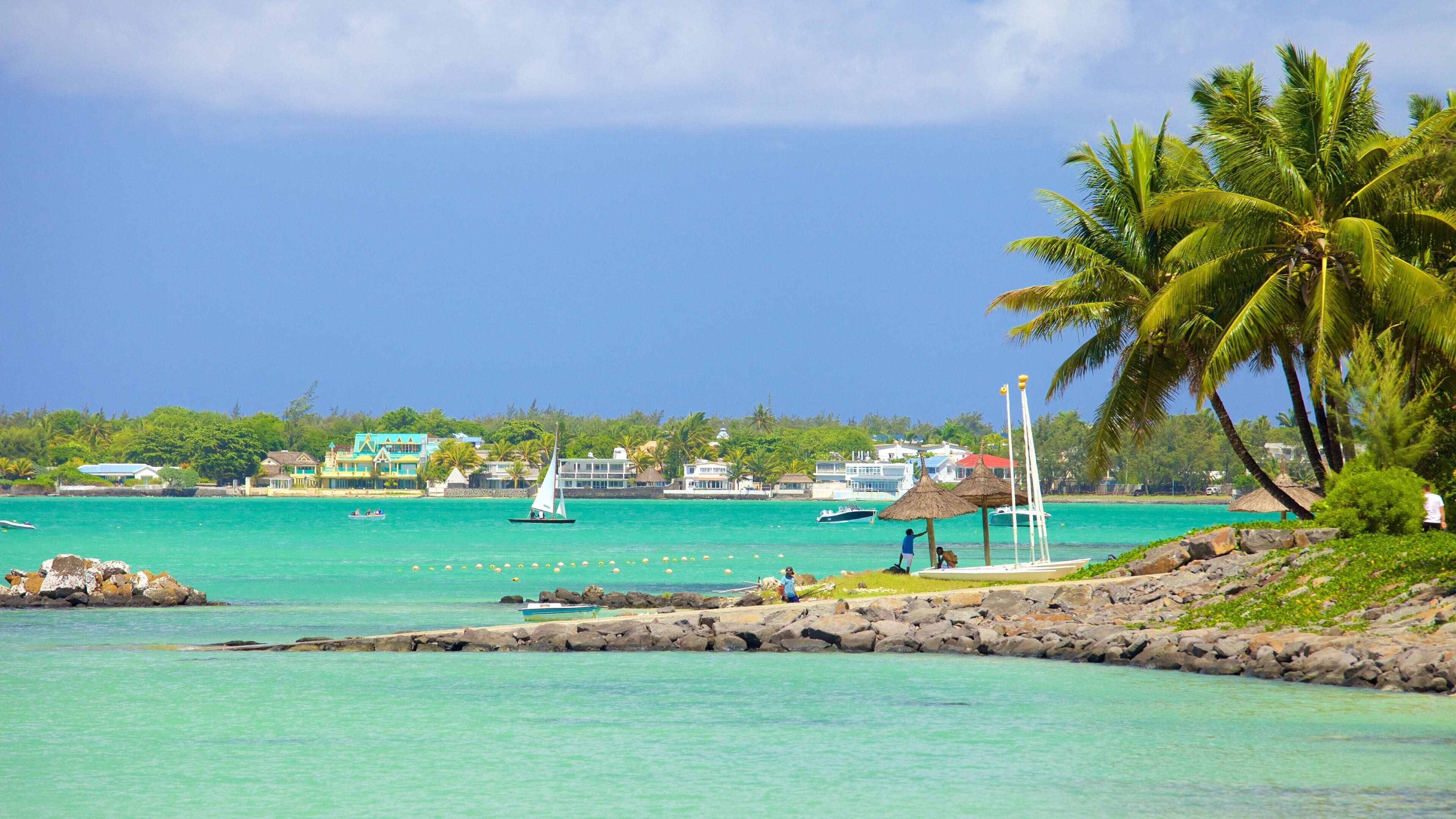 Uma praia tropical com águas azul-turquesa cristalinas, palmeiras e alguns veleiros.