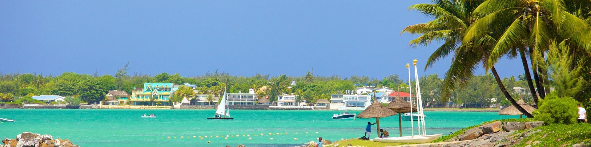 Uma praia tropical com águas azul-turquesa cristalinas, palmeiras e alguns veleiros.