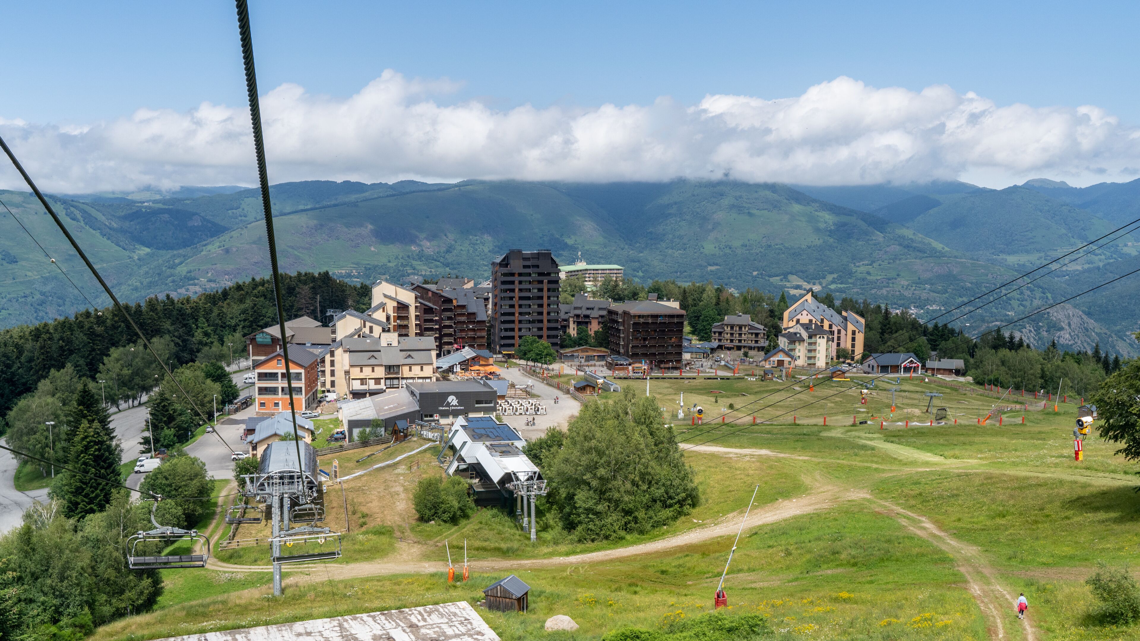 Estância de esqui montanhosa com edifícios, teleférico e céu claro.