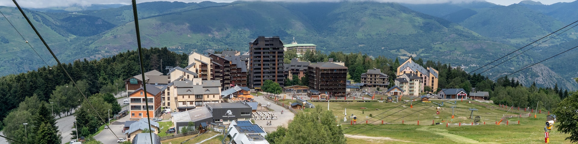 Estância de esqui montanhosa com edifícios, teleférico e céu claro.