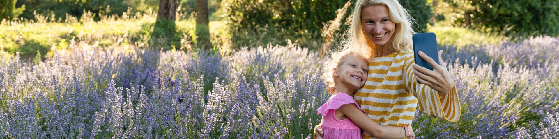 Mulher e criança em um campo de lavanda, com árvores ao fundo.